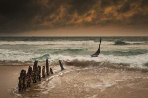 posterazzi wooden posts on a beach with a boat being tossed in the water and waves crashing into the sand under a cloudy sky queensland australia poster print, (38 x 24)