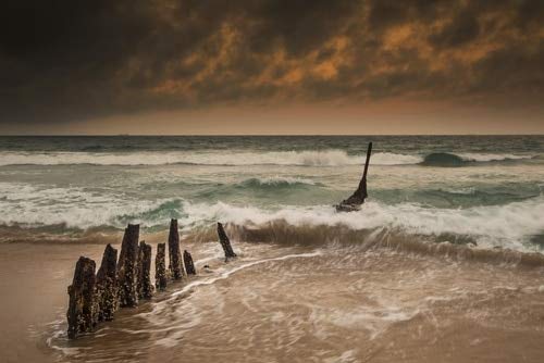 Posterazzi Wooden posts on a beach with a boat being tossed in the water and waves crashing into the sand under a cloudy sky Queensland Australia Poster Print, (38 x 24)